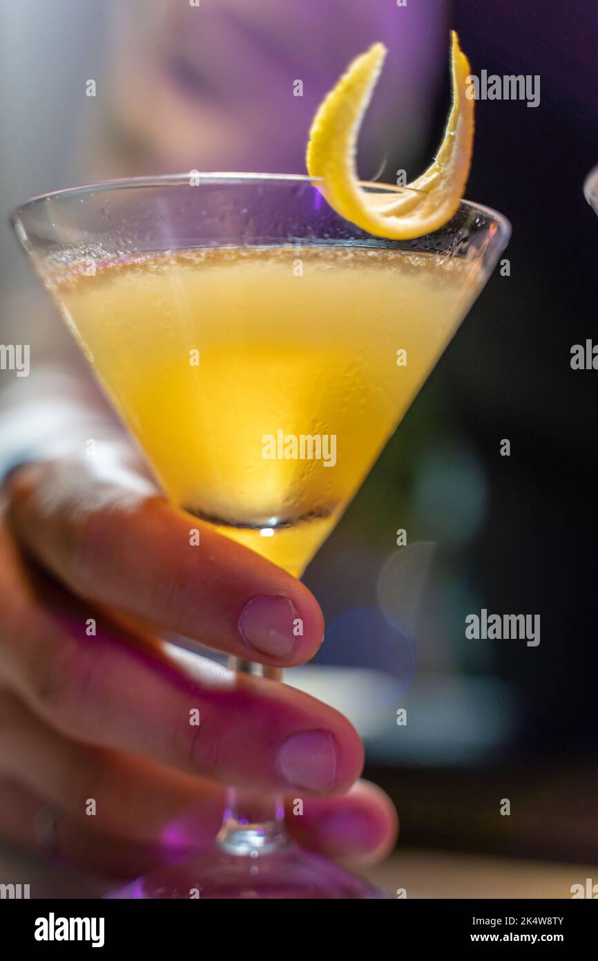 Close-up of a barman's hand serving a beautiful yellow cocktail with ...