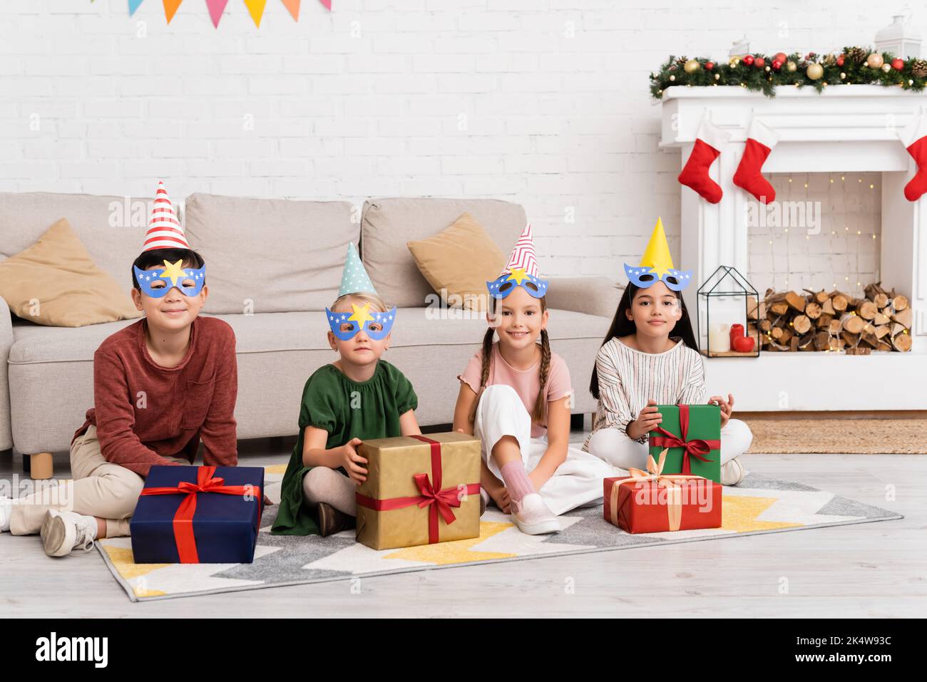 Smiling multiethnic kids in party caps and masks looking at camera near ...
