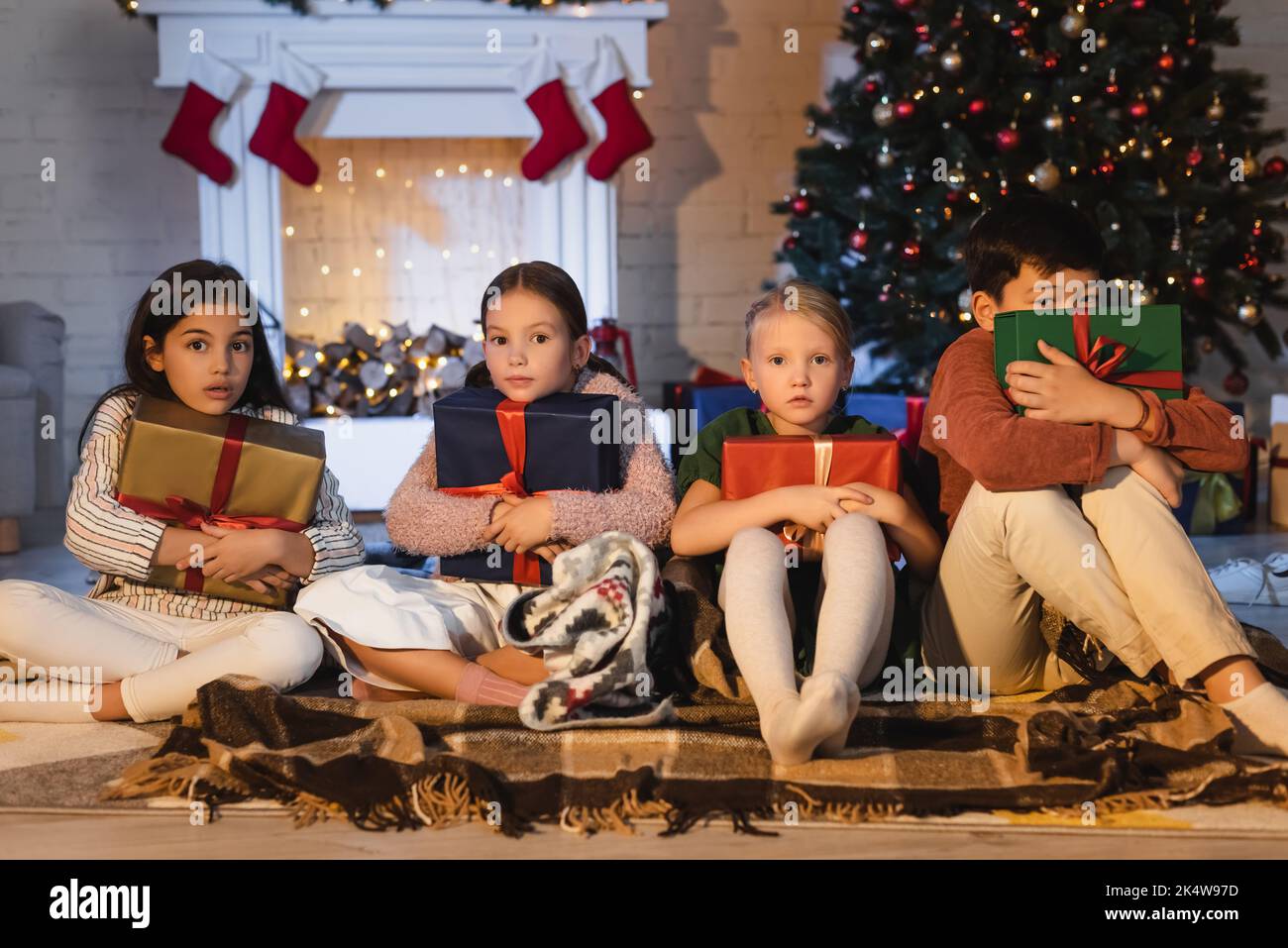 Afraid interracial children holding presents near blurred fireplace and ...