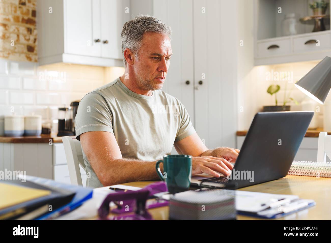 Happy caucasian man sitting at table in kitchen and using laptop Stock ...