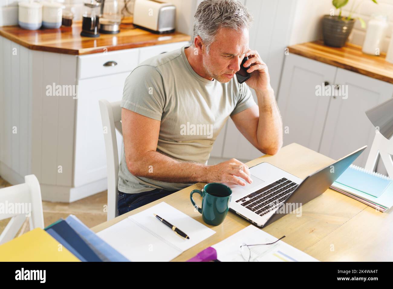 Happy caucasian man sitting at table in kitchen and using laptop and ...