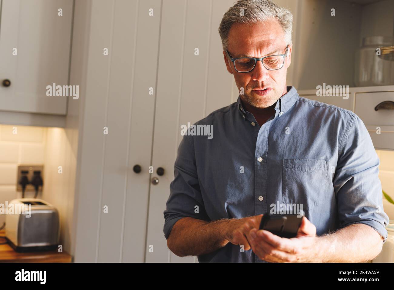 Happy caucasian man standing in kitchen and using smartphone Stock ...