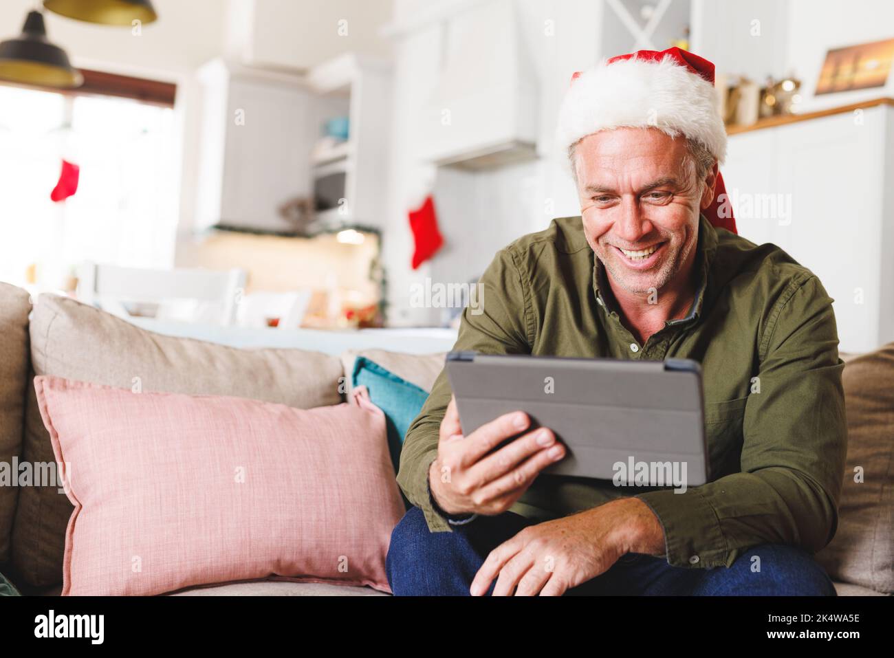 Happy caucasian man wearing santa hat, sitting on sofa in living room ...