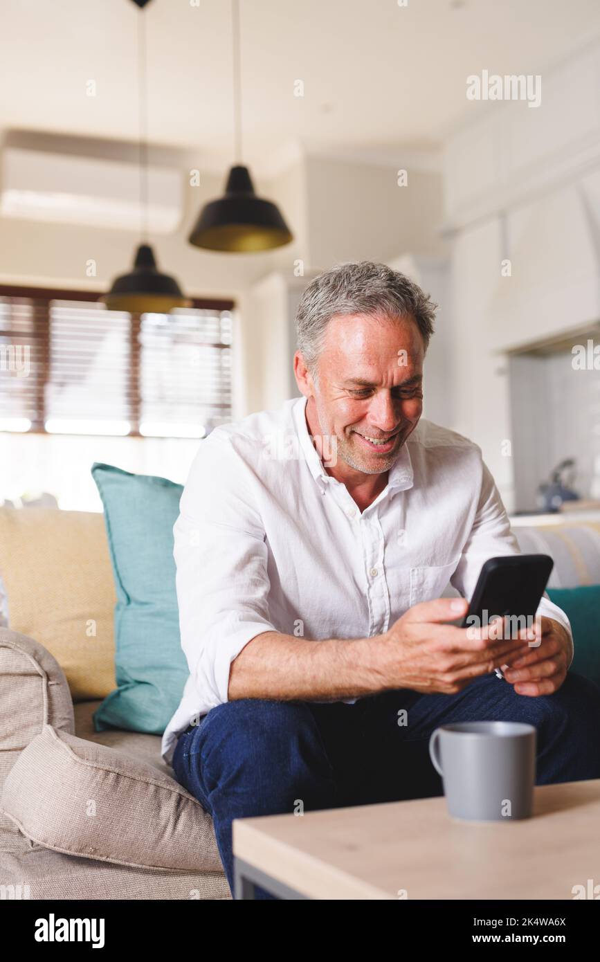 Happy caucasian man sitting on sofa in living room, using smartphone ...