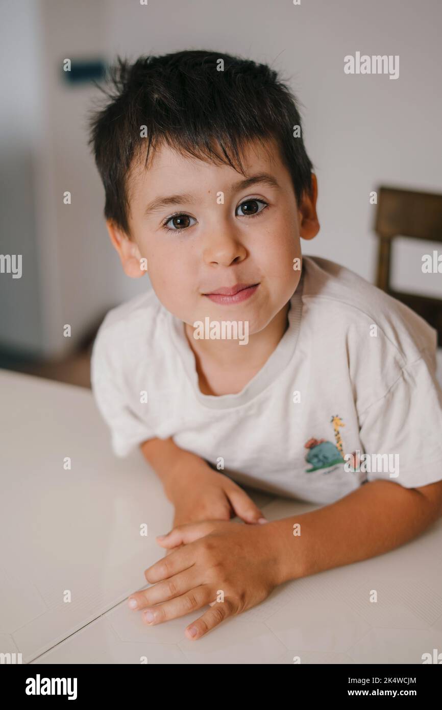 Cute school-age boy sitting at a table in the kitchen, waiting for food ...