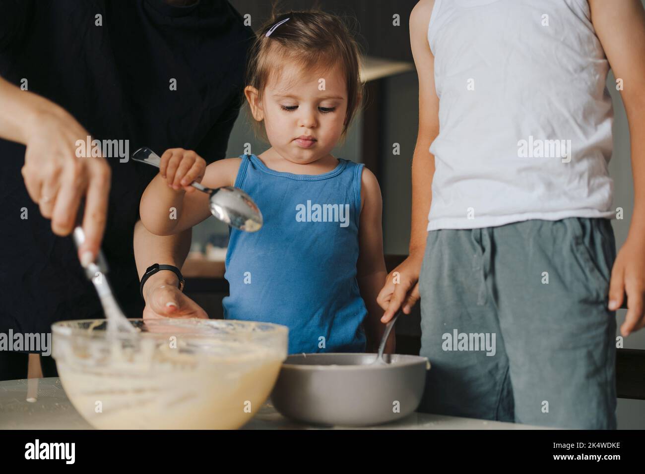 Mother teaching small adorable kids mixing flour with milk, cooking ...