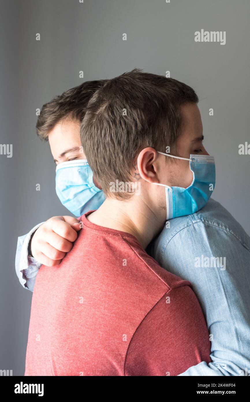 Two men wearing protective disposable face masks hugging each other ...