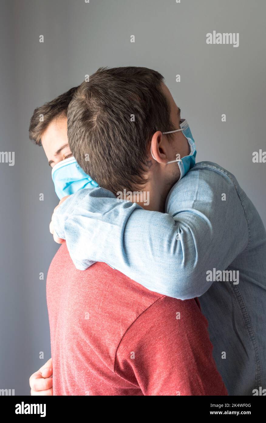 Two men wearing protective disposable face masks hugging each other ...
