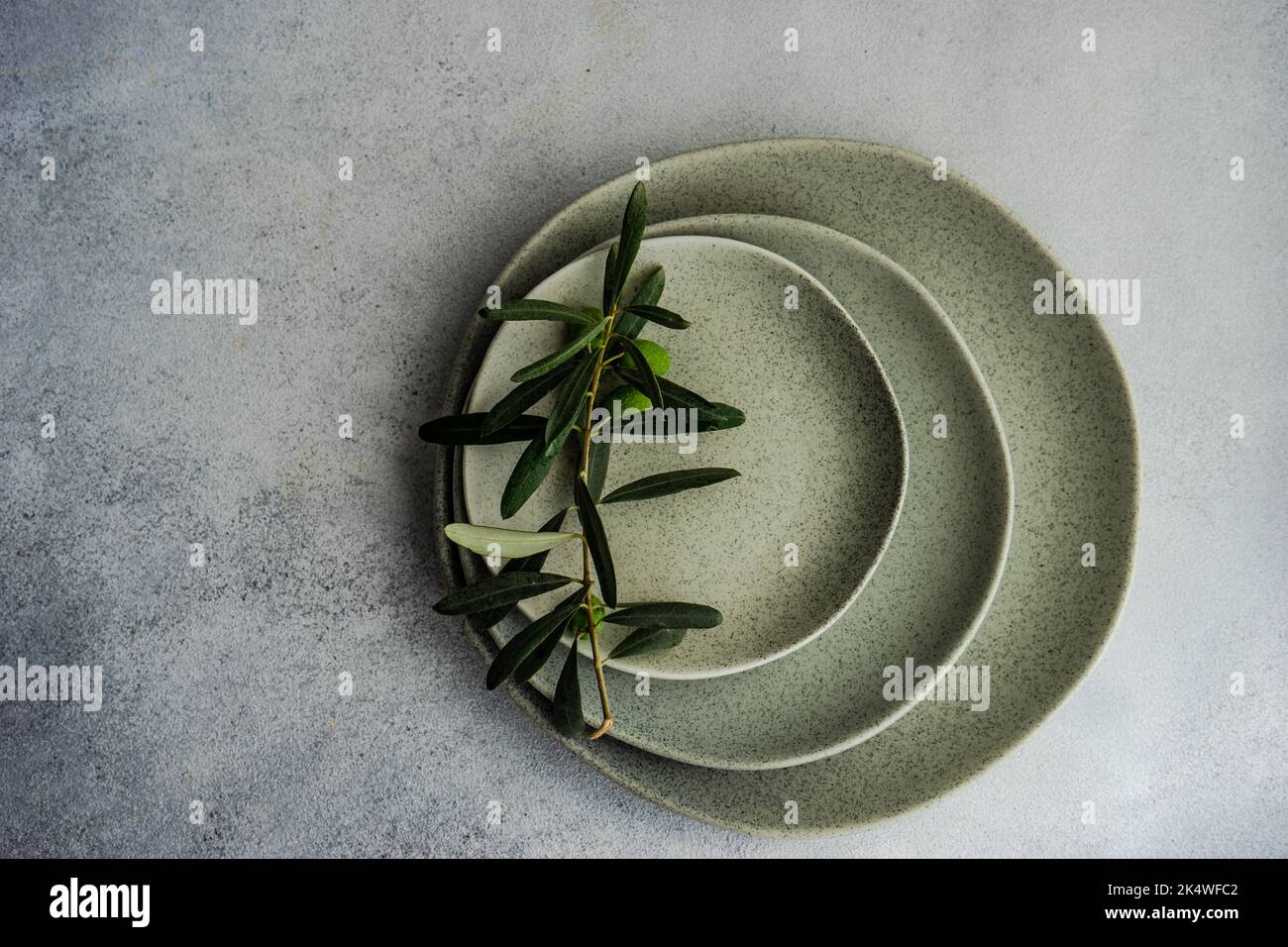 Overhead view of an olive branch on a stack of rustic ceramic plates ...