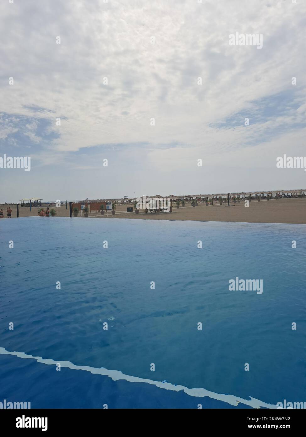 A vertical shot of a pool on the shore of a beach with the sea in the ...