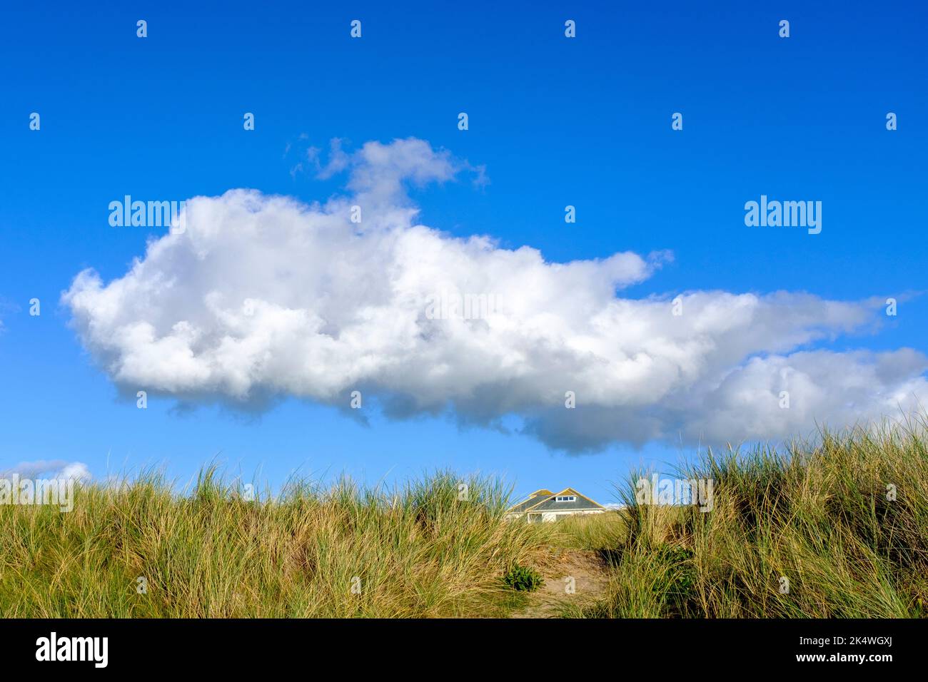 White clouds in a clear blue sky above a simple cottage over the sand ...
