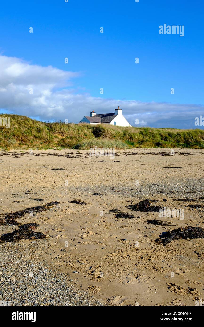 White clouds in a clear blue sky above a simple cottage over the sand ...