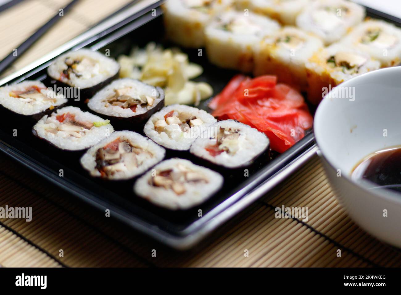 A close up of red ginger rolls with a soy sauce bowl on a bamboo mat ...