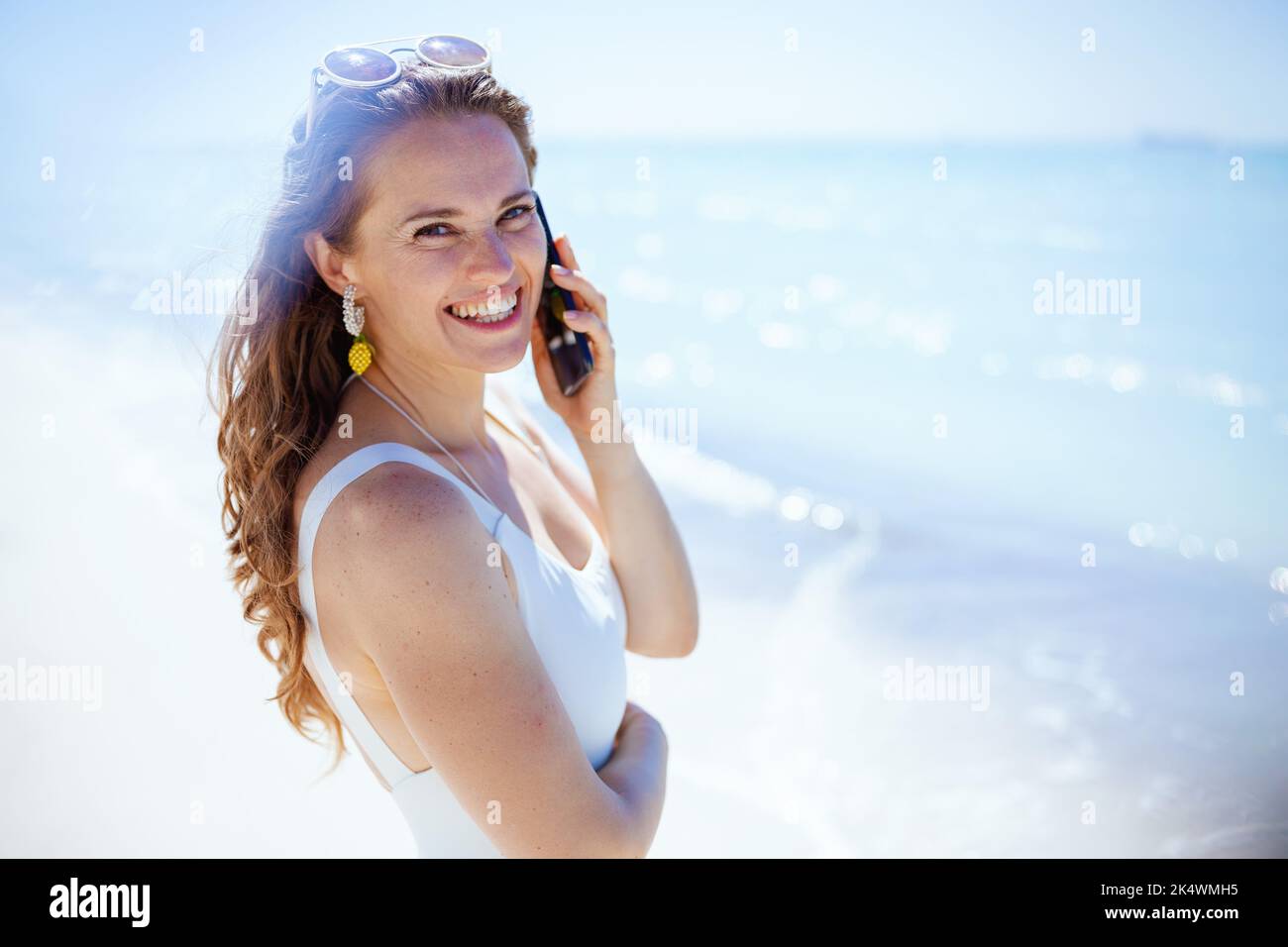 Portrait of happy modern woman at the beach in white swimsuit speaking ...