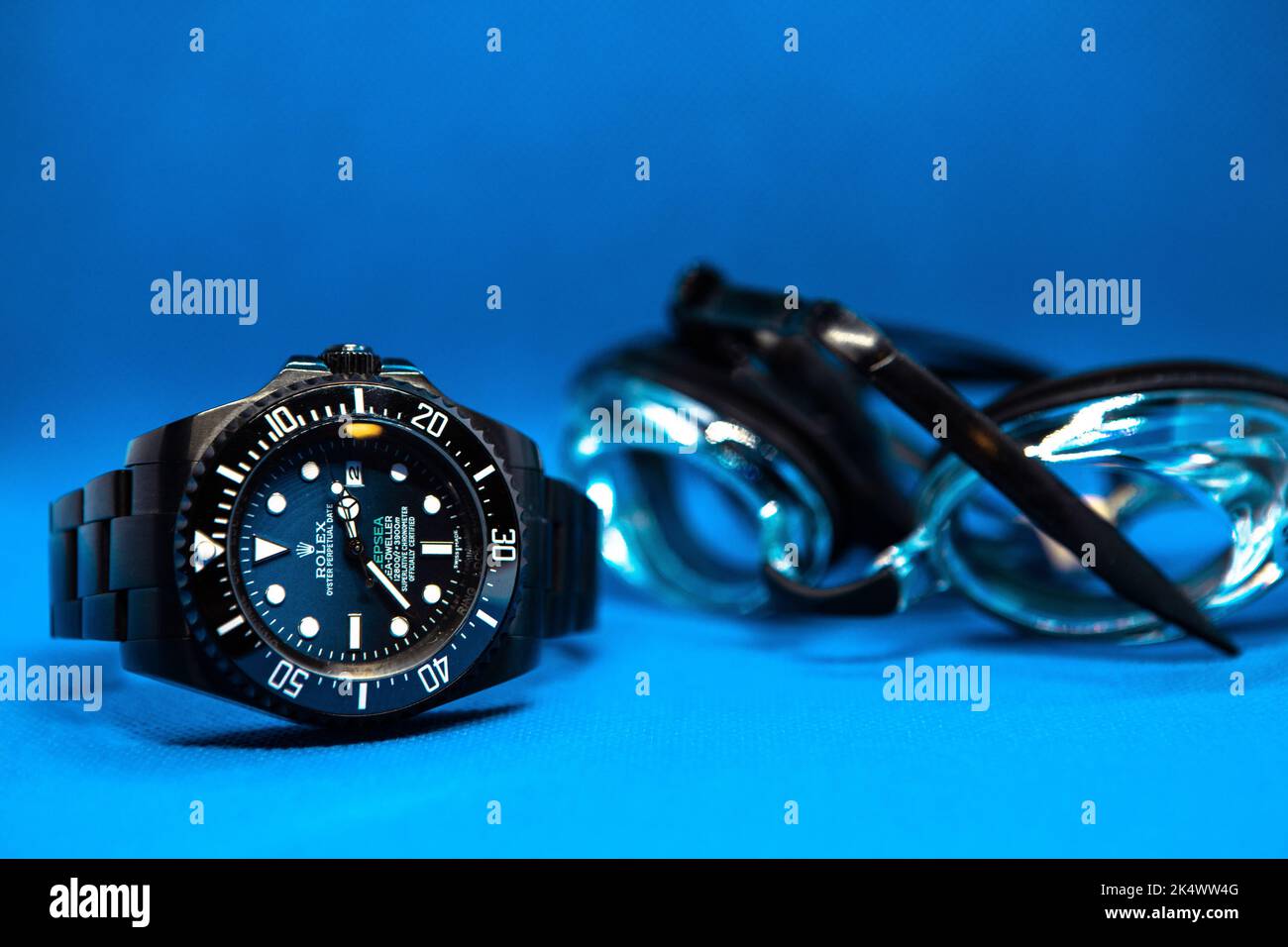 A Rolex luxury watch with a swimming goggles isolated on a blue ...