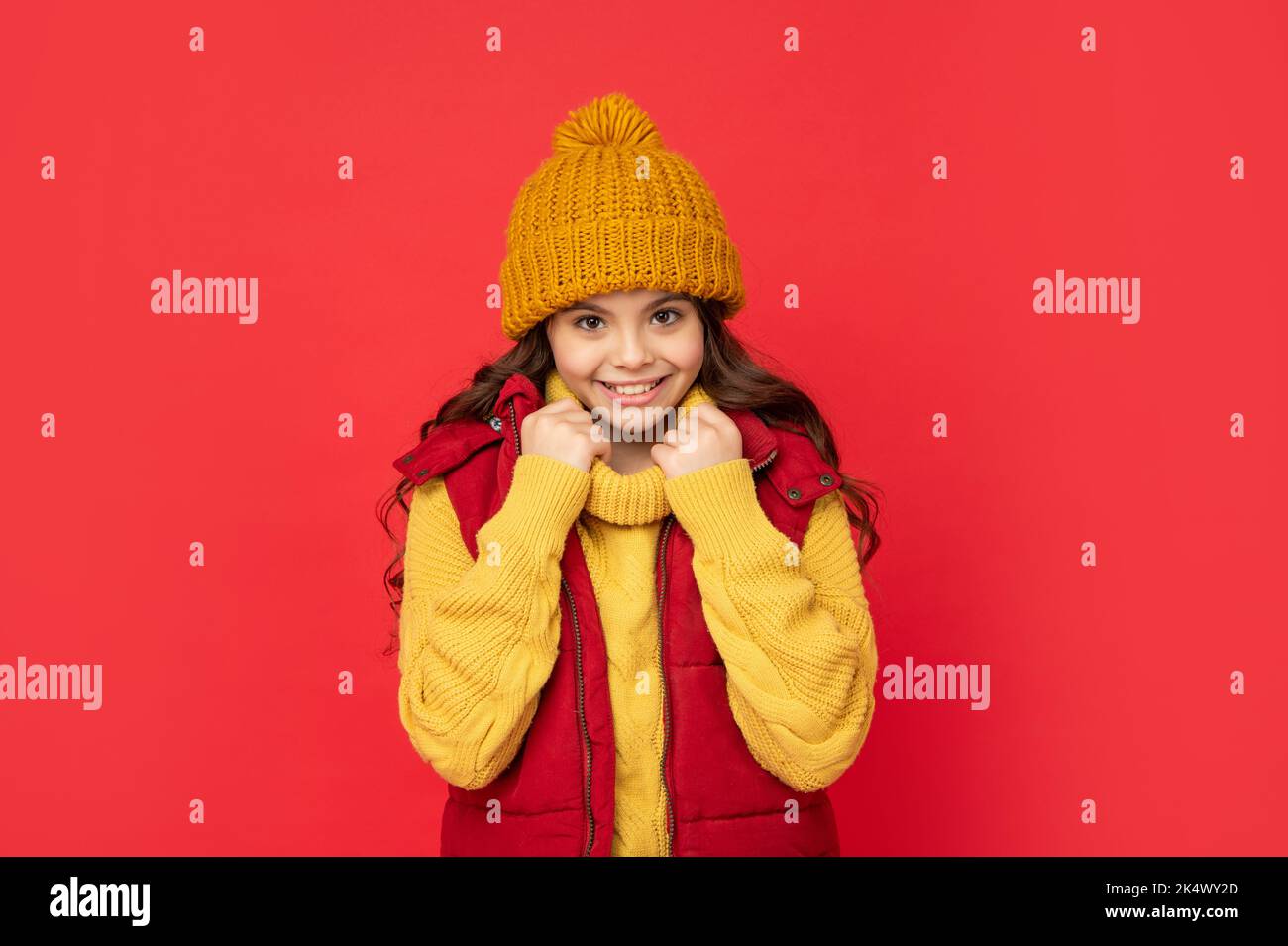 cheerful teen girl in knitted winter hat on red background, autumn ...