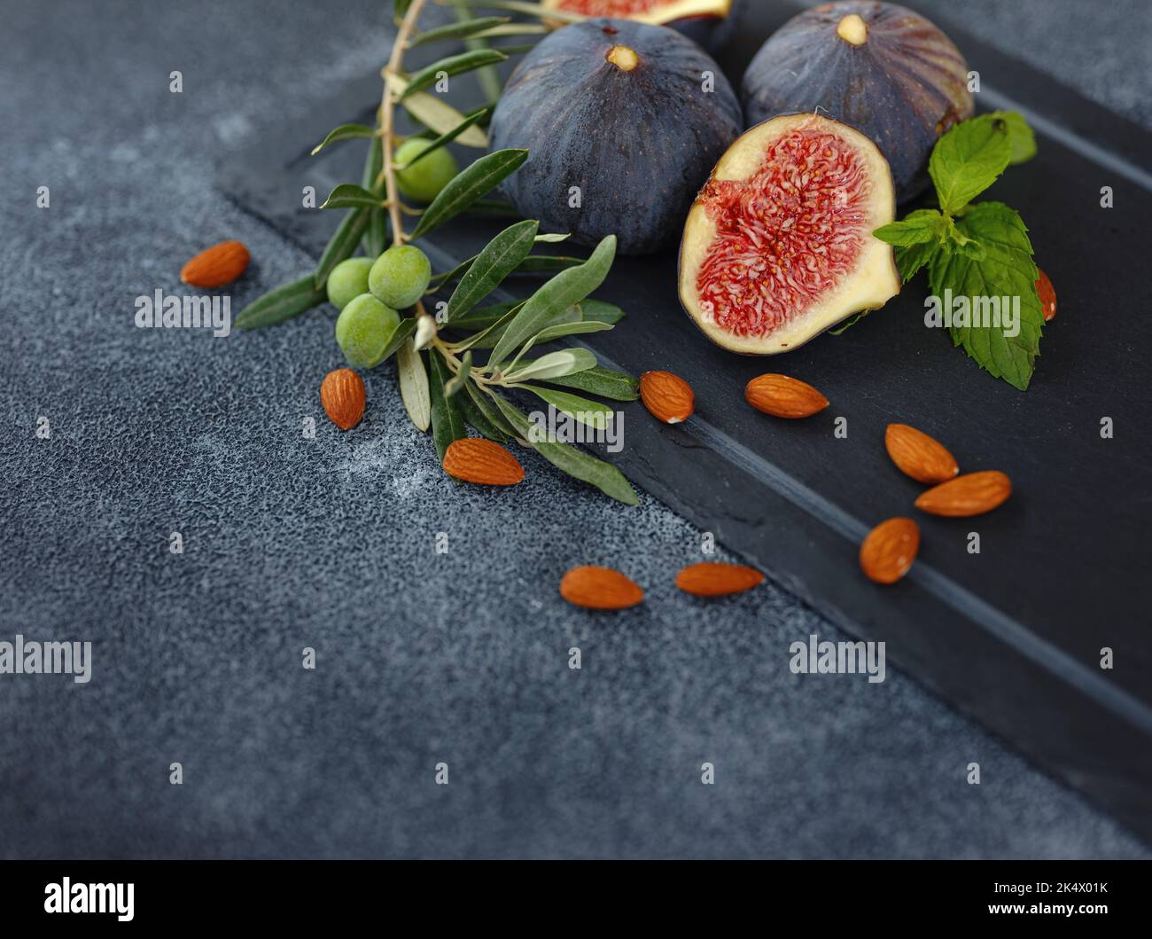 fresh ripe figs fruit almond nuts and olive branch on dark table ...