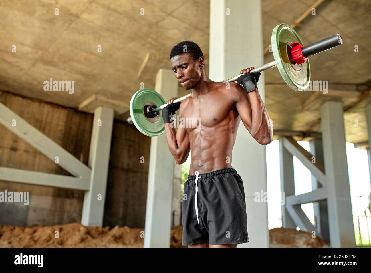 Athletic black young man lifting a heavy-weight barbell in outdoor gym ...