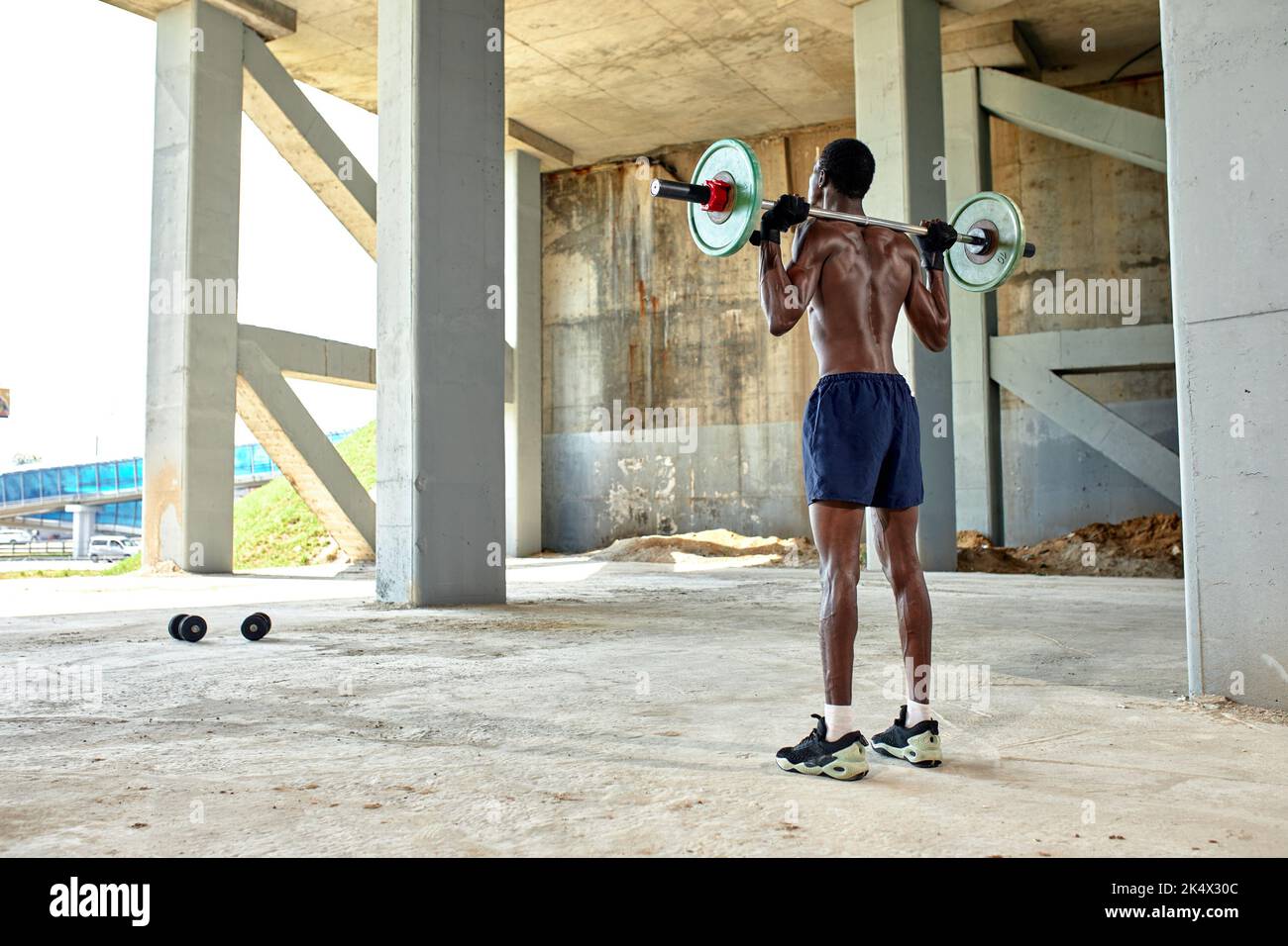 Athletic black young man lifting a heavy-weight barbell in outdoor gym ...