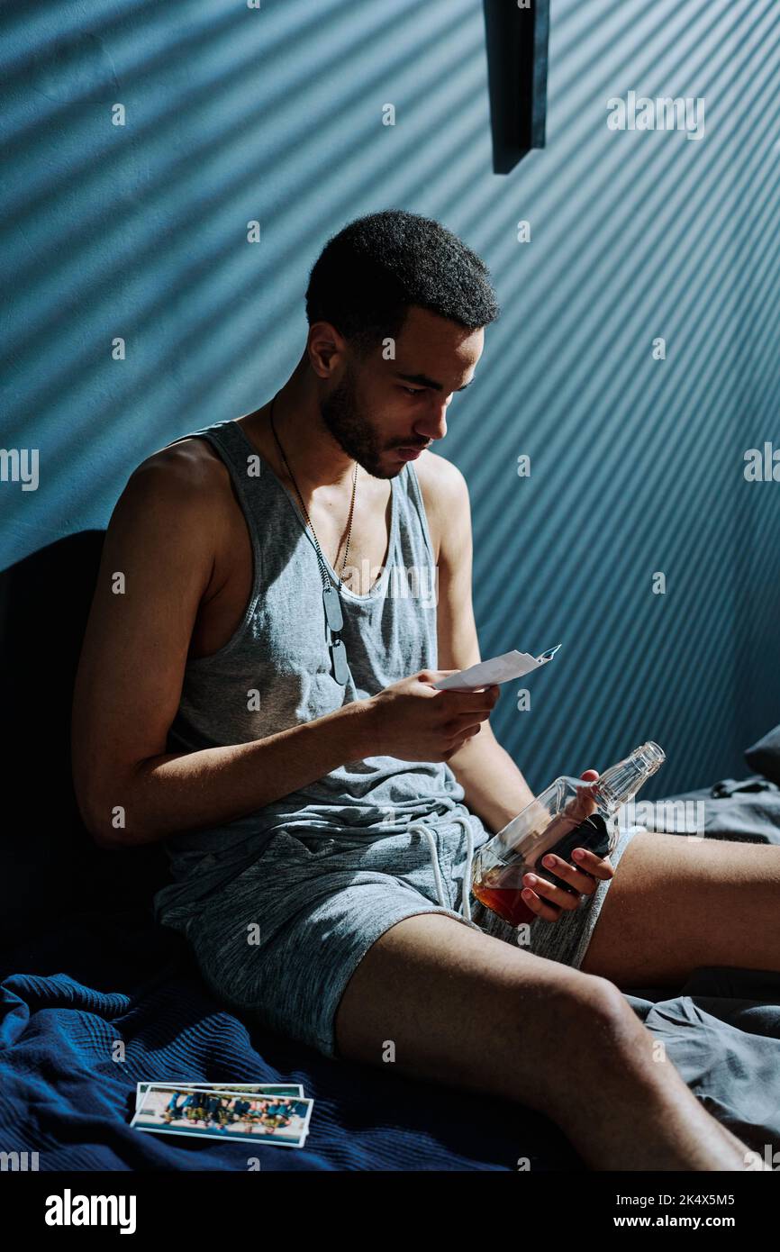 Sad young man having whisky and looking through photos of him and his ...