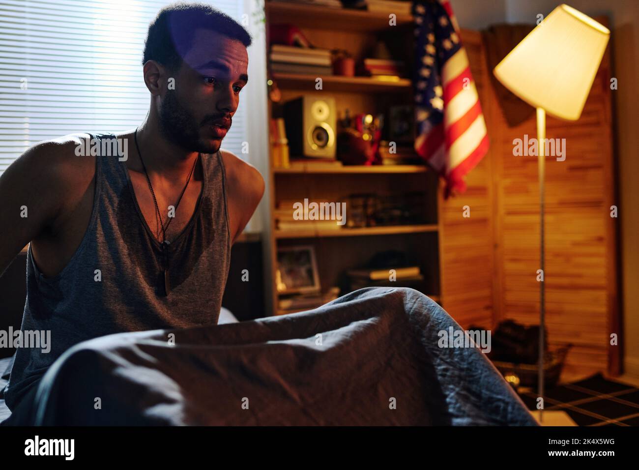 Young scared to death man with post traumatic syndrome sitting on bed ...