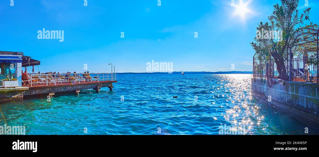 The bright blue sky with evening sun over Lake Garda with azure rippled ...