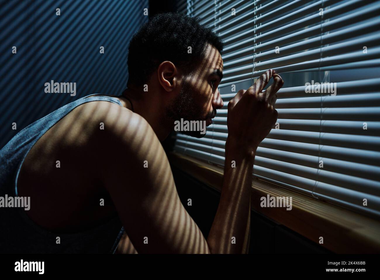 Side view view of young sleepless man looking through venetian blinds ...