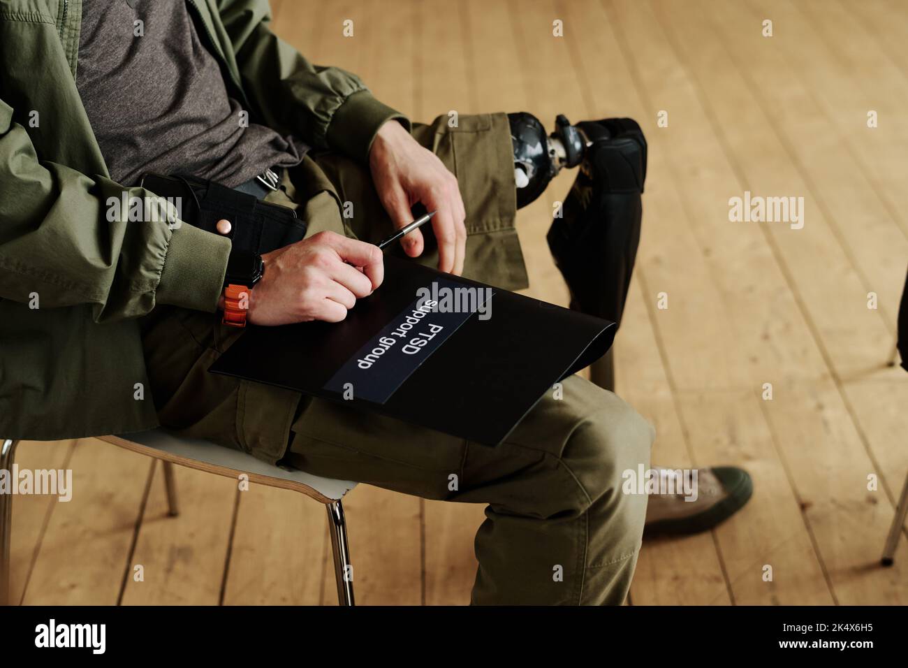 Young man with disability holding black folder of PTSD support group ...