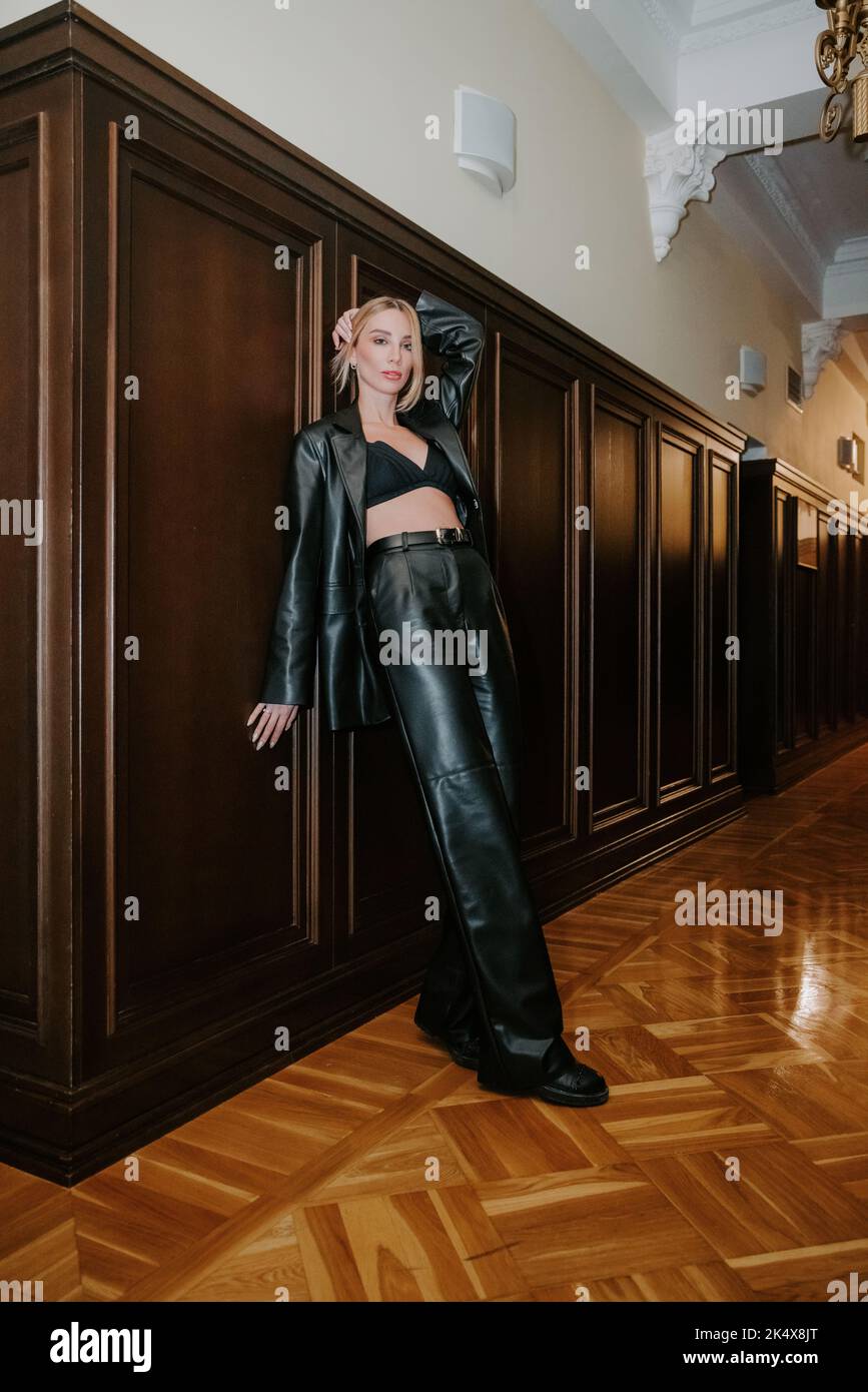 Pretty slim lady wearing a dark leather suit leaning against a wall ...