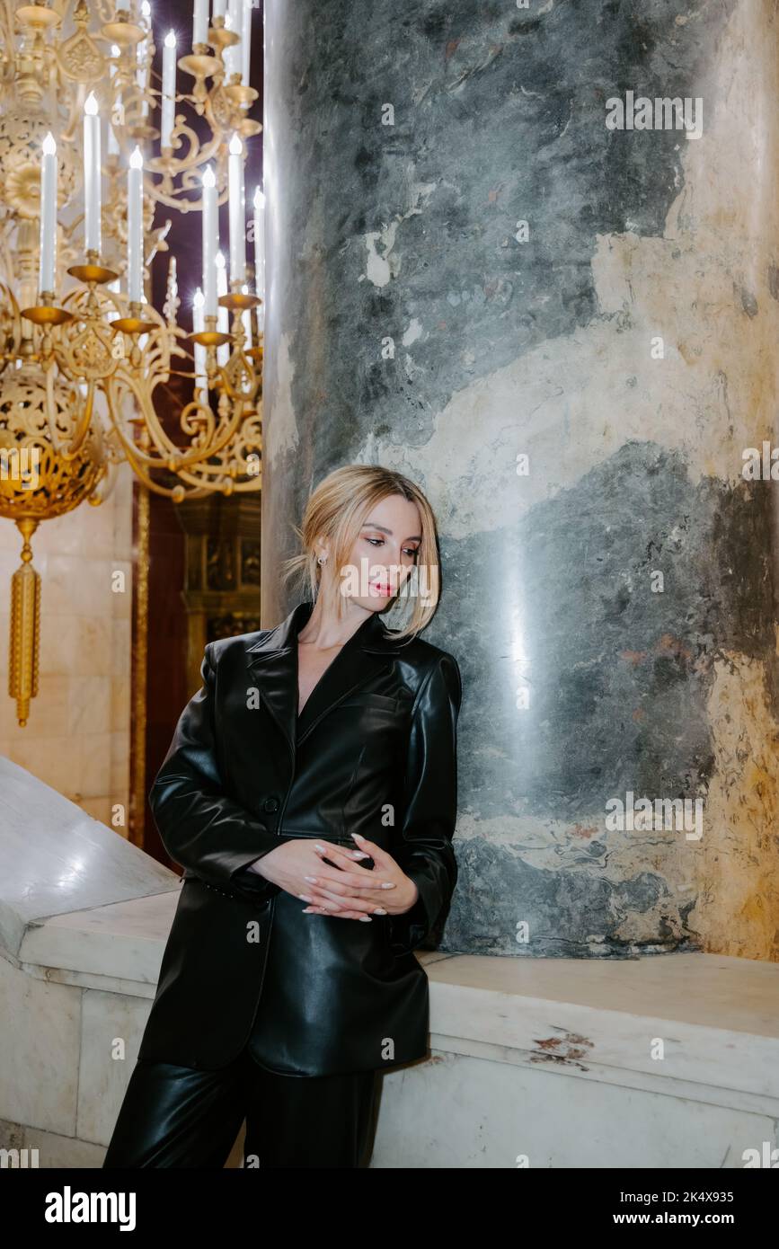 Pretty slim lady wearing a dark leather suit leaning against a marble ...