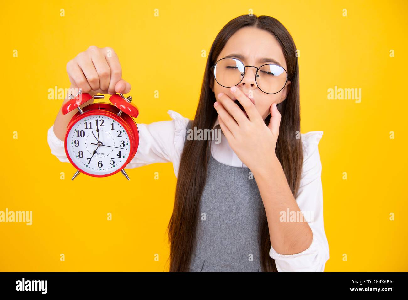 Tired and bored teenager student girl hold clock isolated on yellow ...