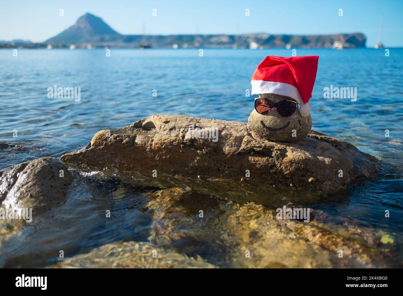 Stone with a smile and in a Santa red hat is laying on a big rock Stock ...