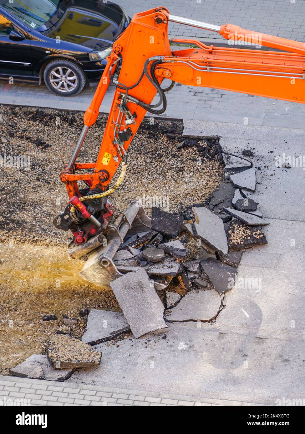 An excavator breaks up the old asphalt layer with a bucket during ...