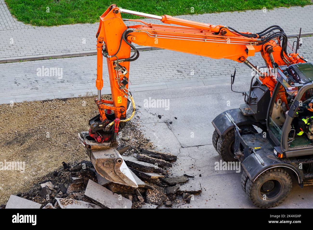 An excavator breaks up the old asphalt layer with a bucket during ...