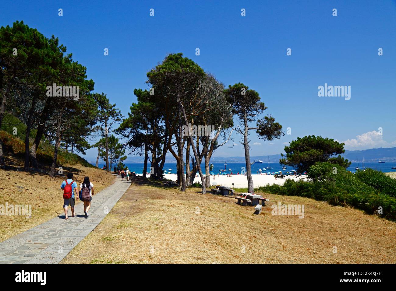 Tourists walk along a path next to the famous Playa de Rodas beach on ...