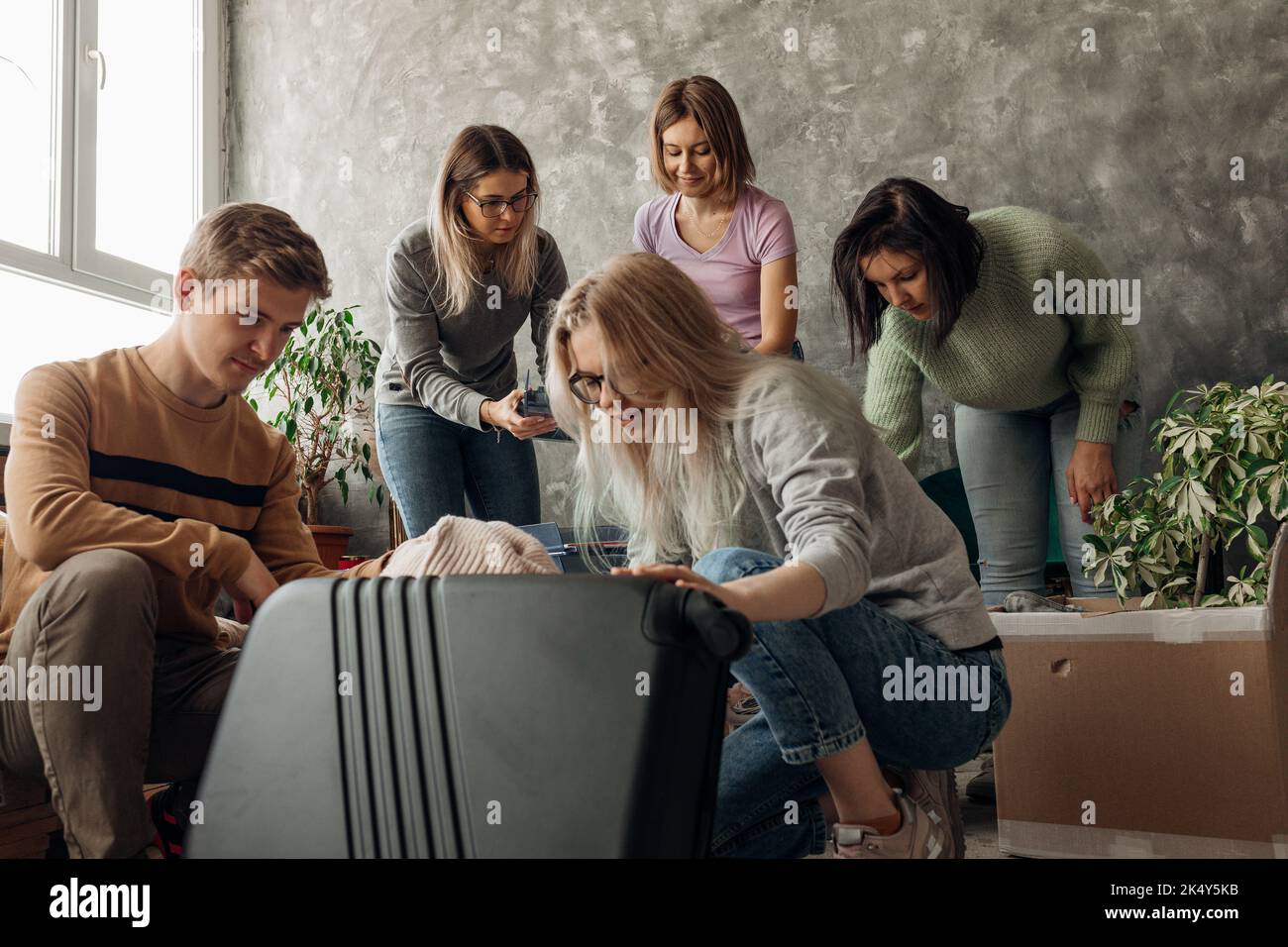 Smiling busy friends packing luggage and trying to fit things in ...
