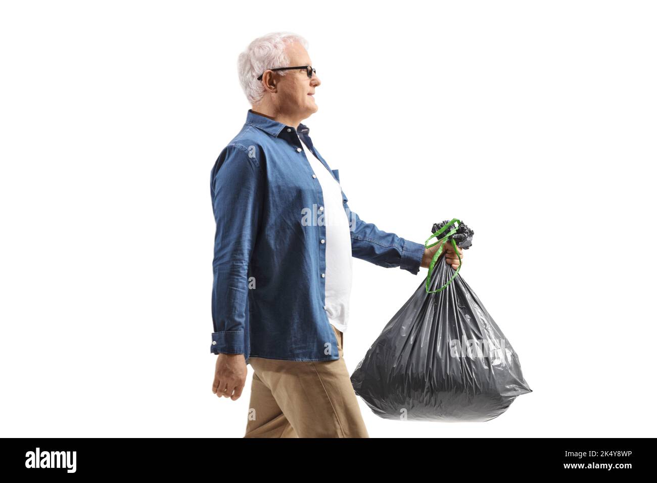 Profile shot of a mature man walking and carrying a plastic waste bag ...