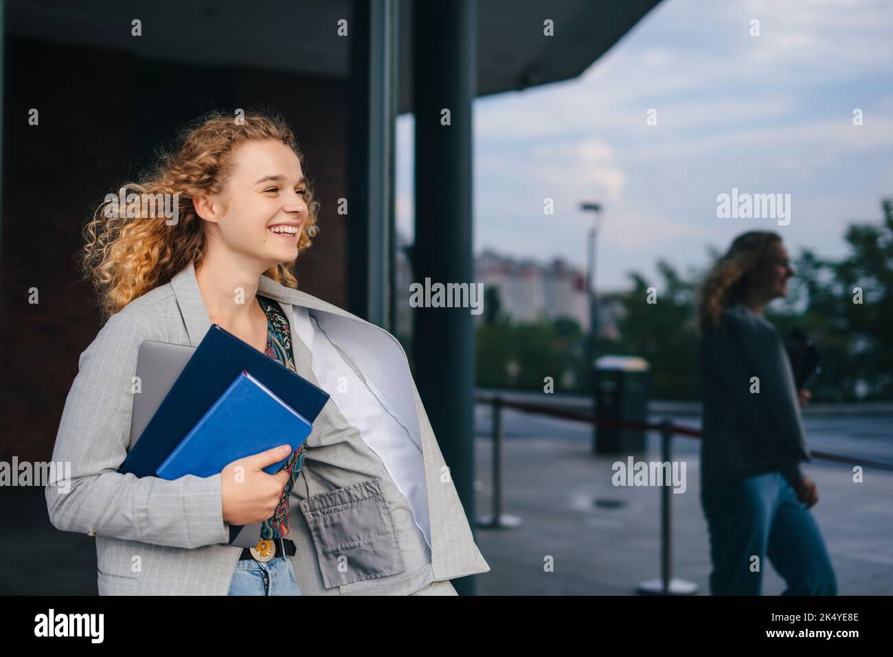 Portrait of beautiful young woman holding papers and laptop walking ...