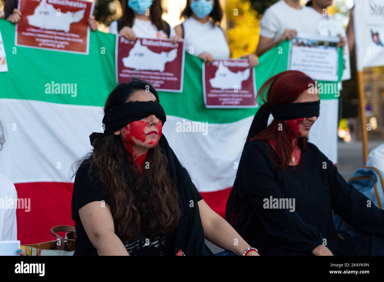 Women sit blindfolded and painted in red against the Iranian flag in ...