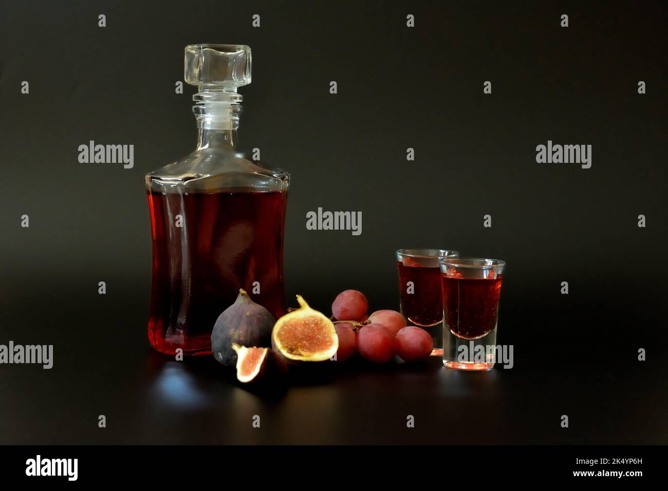 Fig-grape liqueur in a bottle and two glasses on a black background ...