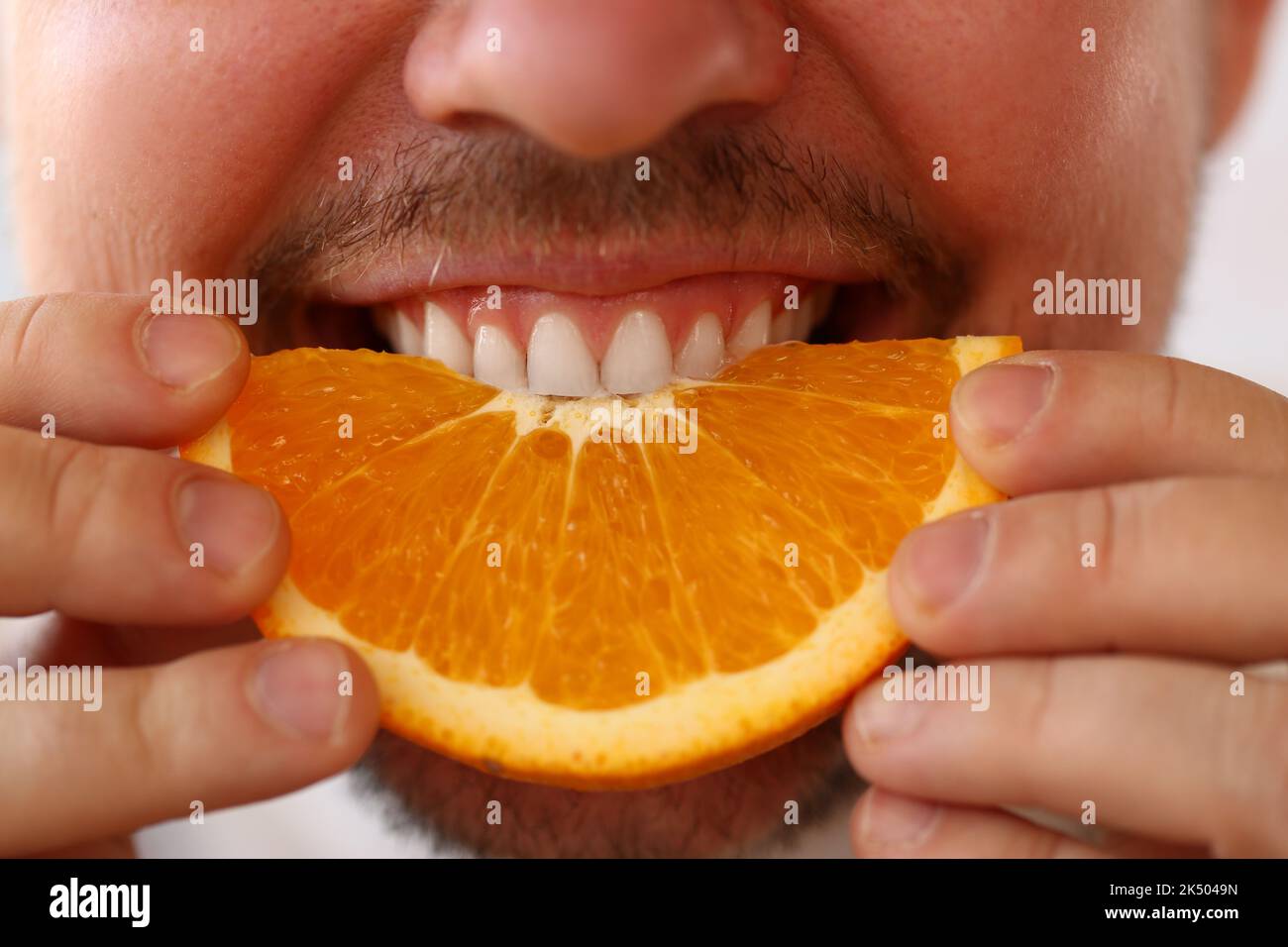 Bearded smiling man holds and bites orange fruit Stock Photo - Alamy