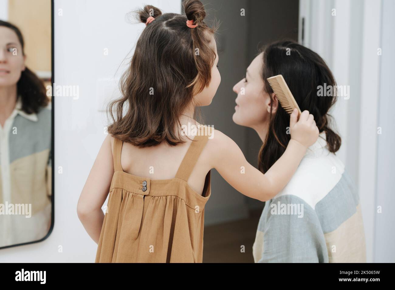 Pretty little girl brushing mother's hair in front of a mirror, face in ...