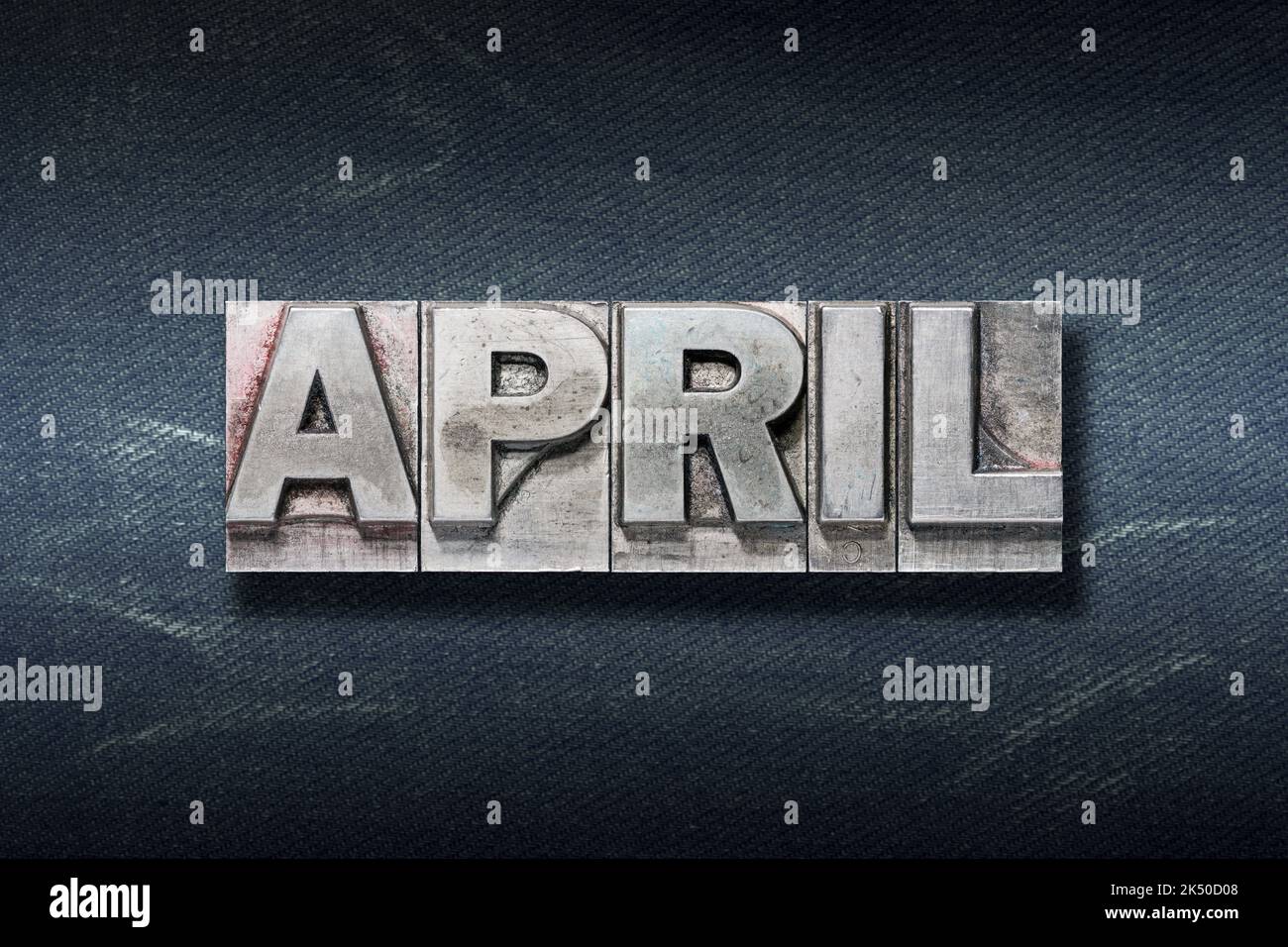 April word made from metallic letterpress on dark jeans background ...