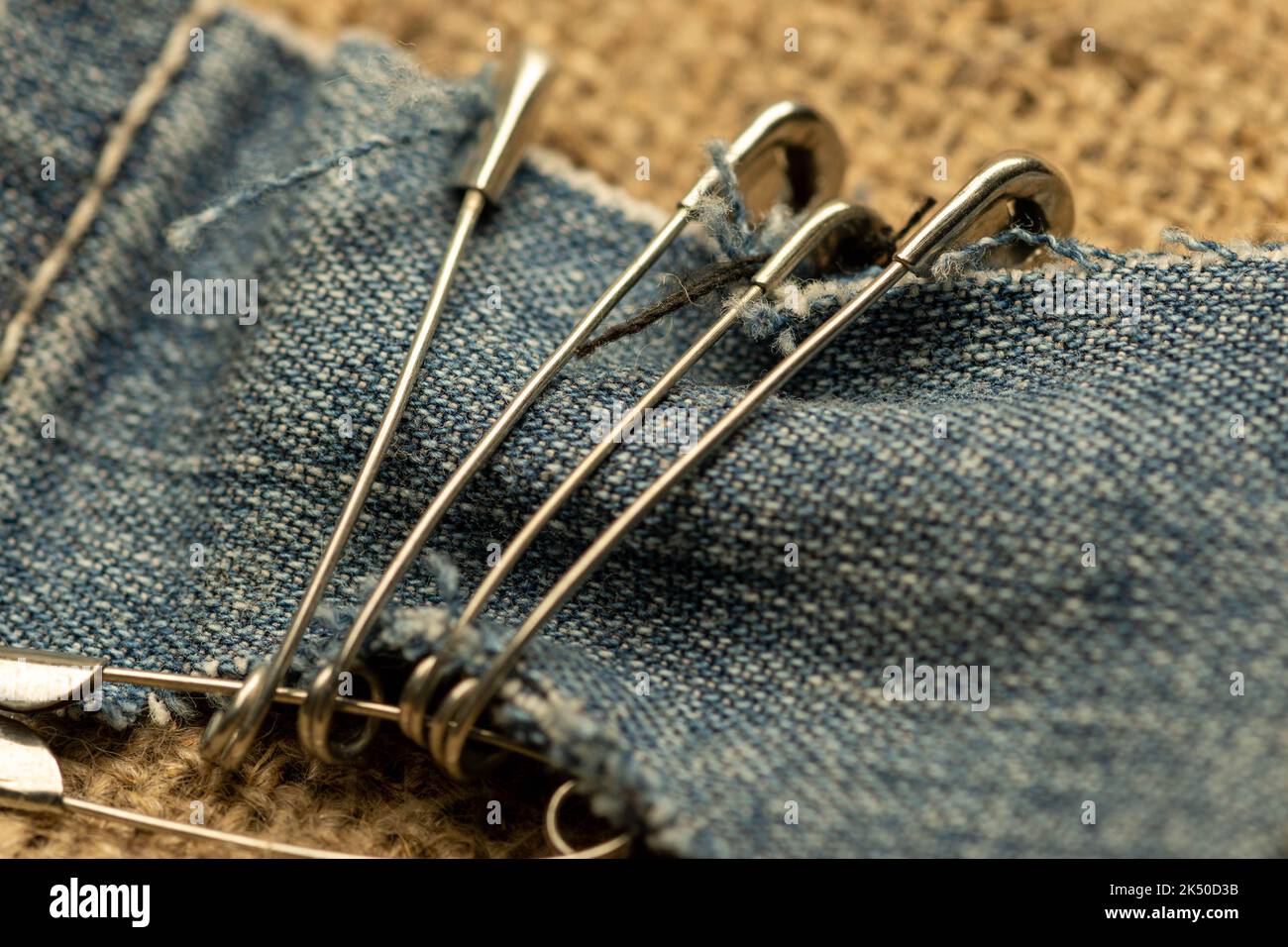 Safety pins on a strip of denim against a homespun fabric with a rough ...