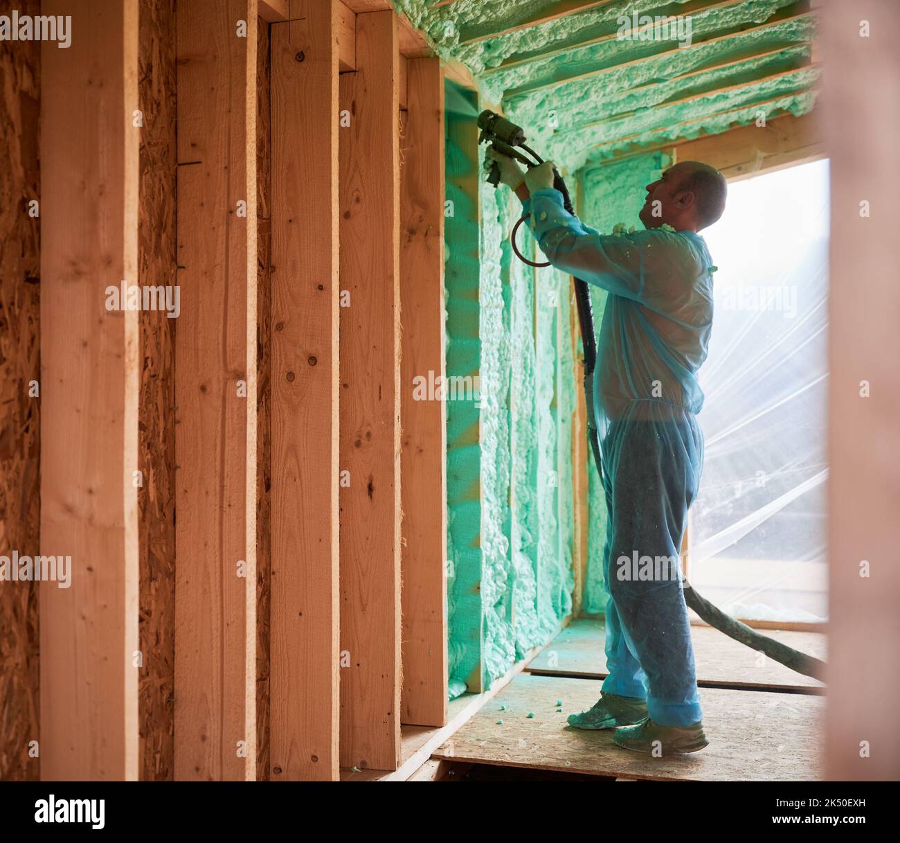 Male builder insulating wooden frame house. Man worker spraying ...