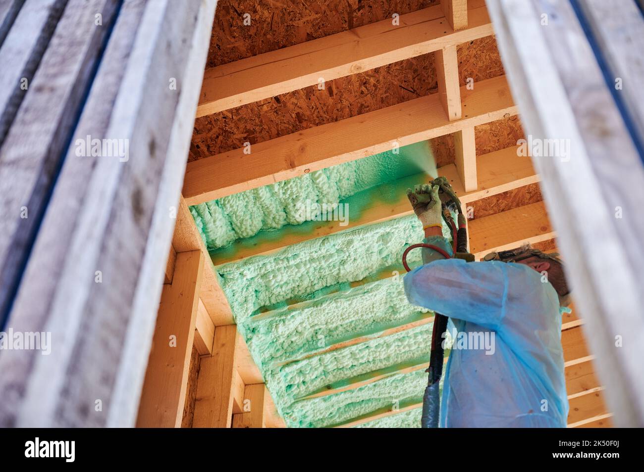 Male builder insulating wooden frame house. Man worker spraying ...