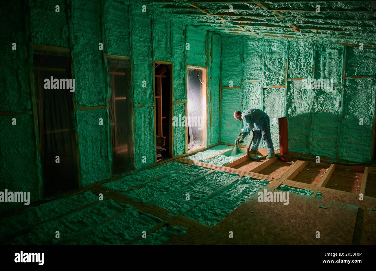 Male builder insulating wooden frame house. Man worker spraying ...