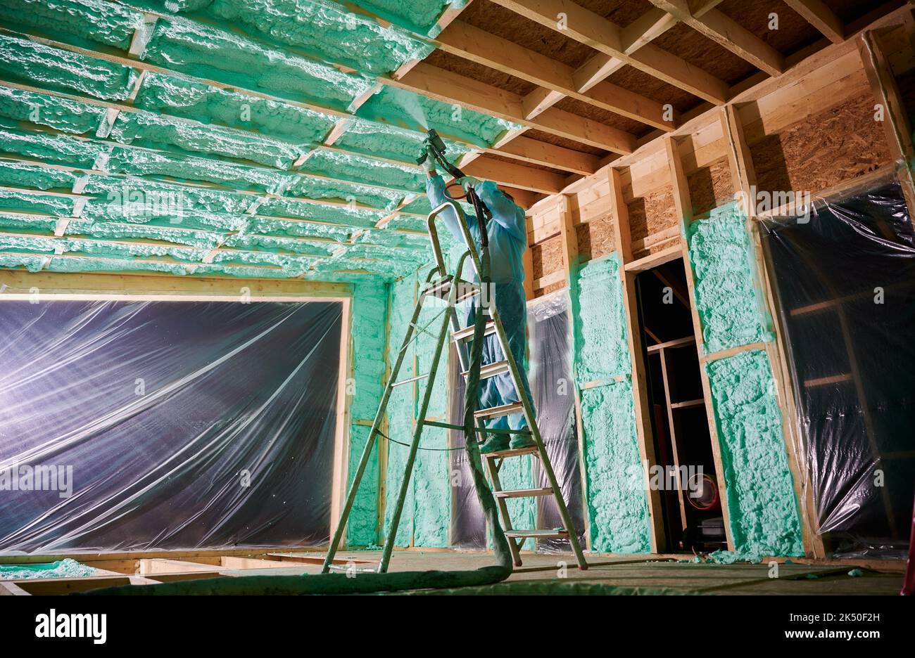 Male builder insulating wooden frame house. Man worker spraying ...