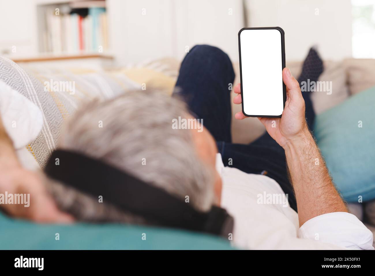 Caucasian man laying on sofa in living room and using smartphone with ...