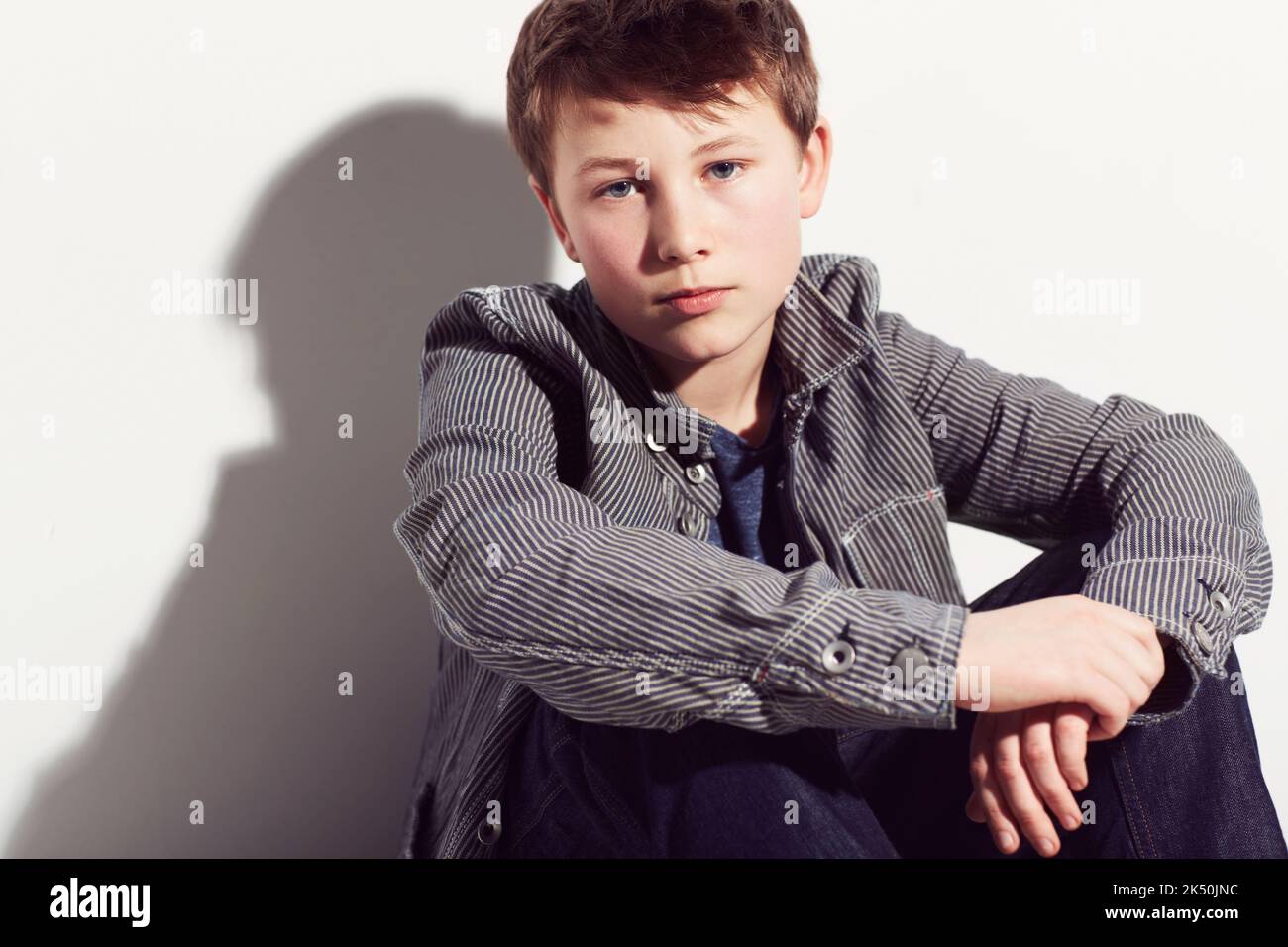 Keeping things casual. Young adolescent boy sitting against a white ...
